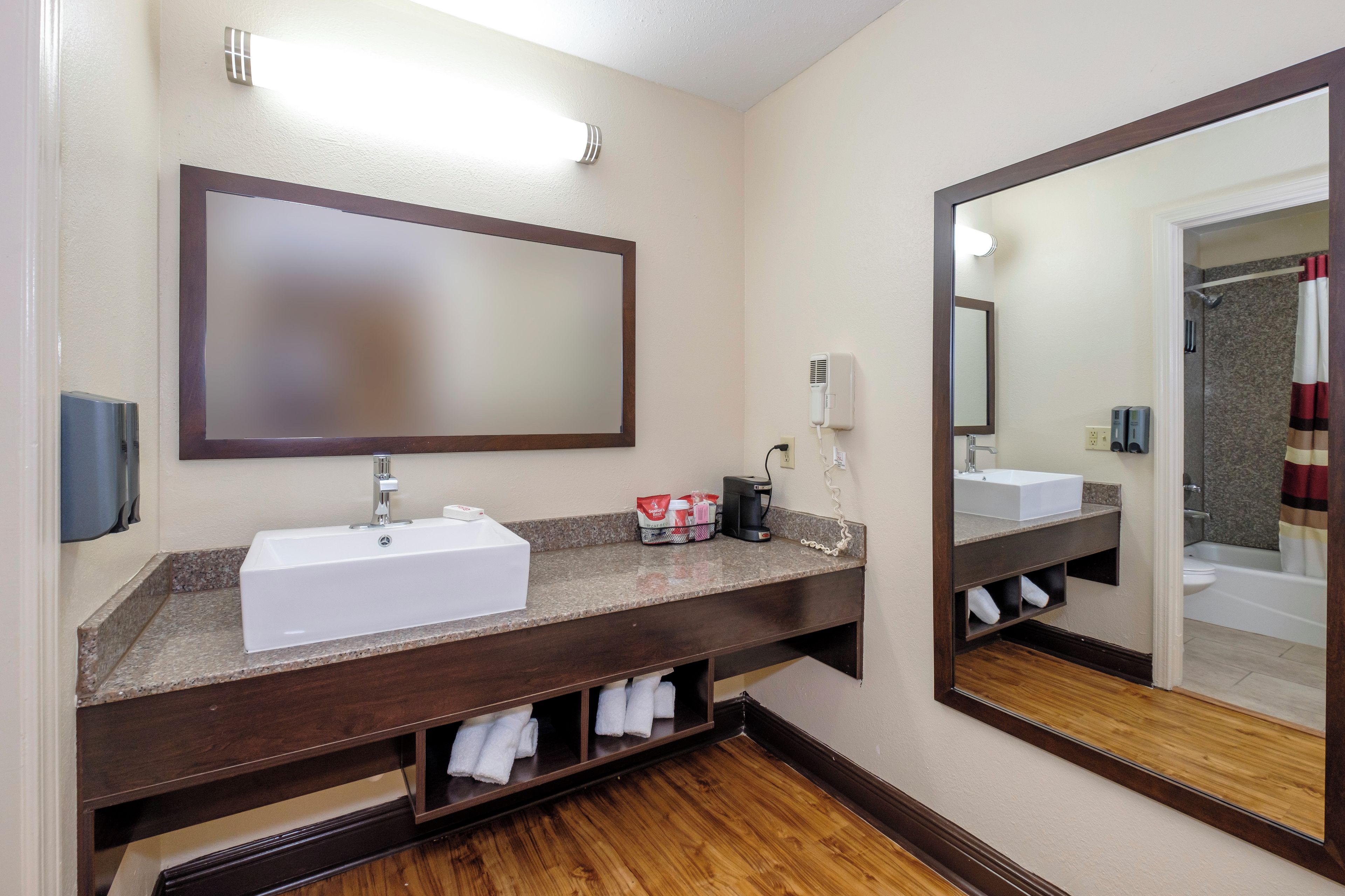 Casa de banho de hotel com um espelho grande, lavatório, porta-toalhas e zona de duche.