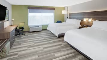 Quarto de hotel com duas camas, uma escrivaninha, uma cadeira, uma televisão e uma janela com ar condicionado.