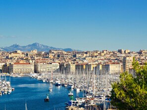 Uma marina cheia de barcos, um horizonte urbano com edifícios históricos e montanhas ao fundo.