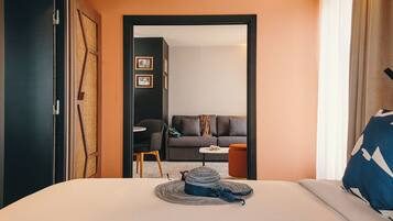 Quarto de hotel com cama, uma cadeira, mesa pequena e sofá ao fundo.