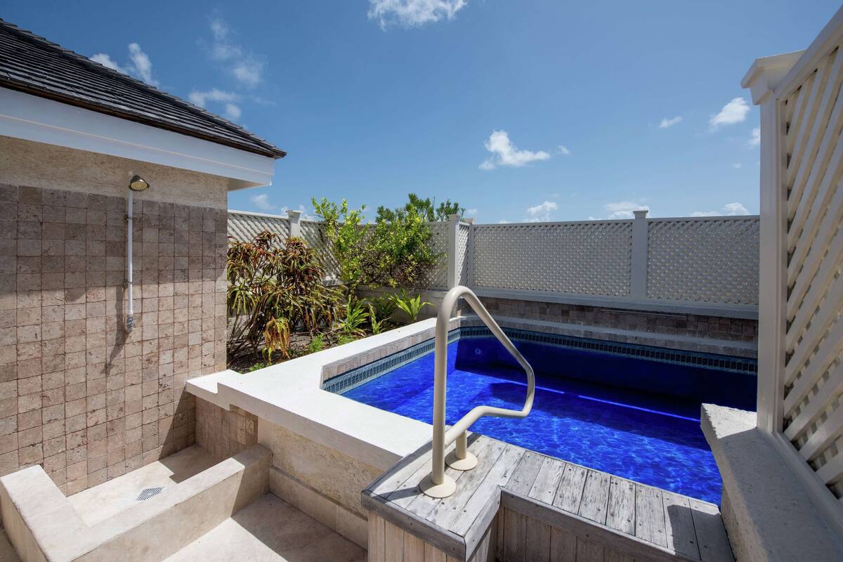 Piscina com degraus para acesso, cercada por um muro branco e uma parede de tijolos.