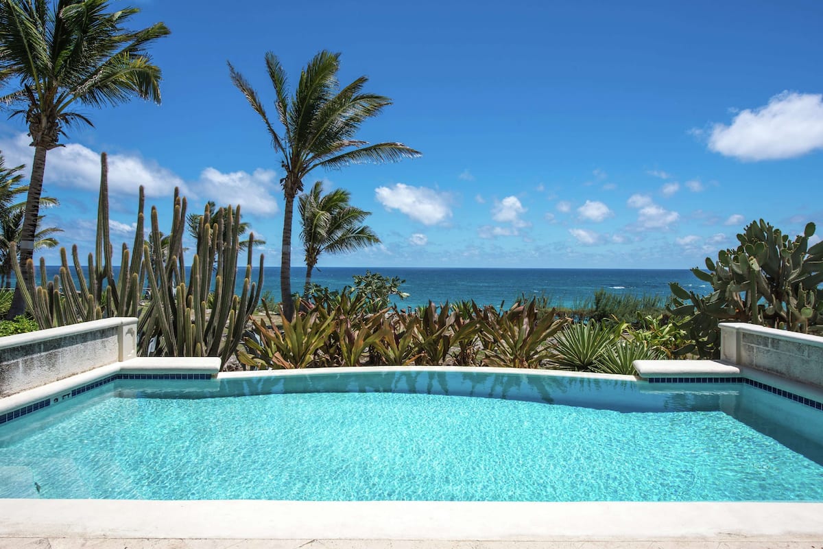 Piscina azul e límpida com vista para o oceano e palmeiras.