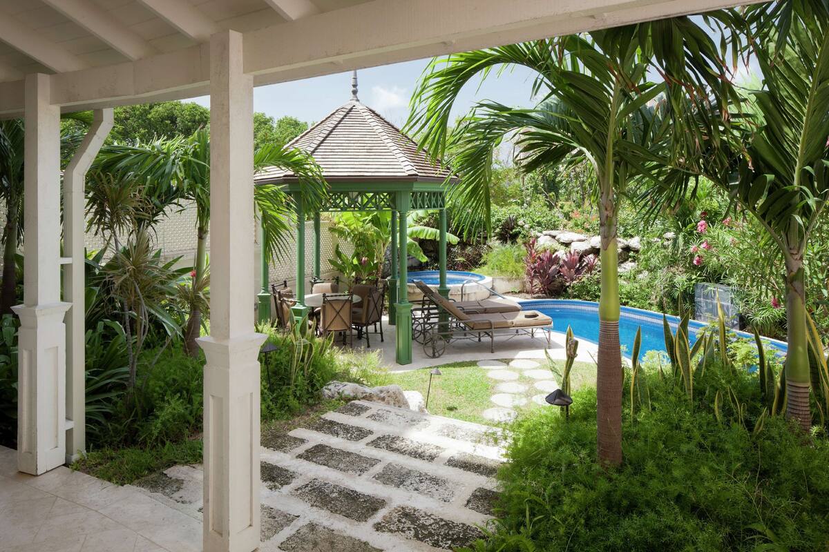 Uma área de varanda coberta com um gazebo, cadeiras de descanso e piscina.