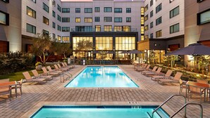 Um hotel moderno com piscina, espreguiçadeiras e fachada bem iluminada.