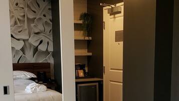 Quarto de hotel moderno com uma cama grande, uma pequena escrivaninha, um espelho e uma porta para o banheiro.