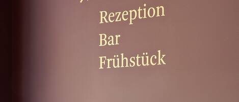 Uma escada com uma placa indicando direções para o Bar da Recepção 1.0G e Fruhstück.