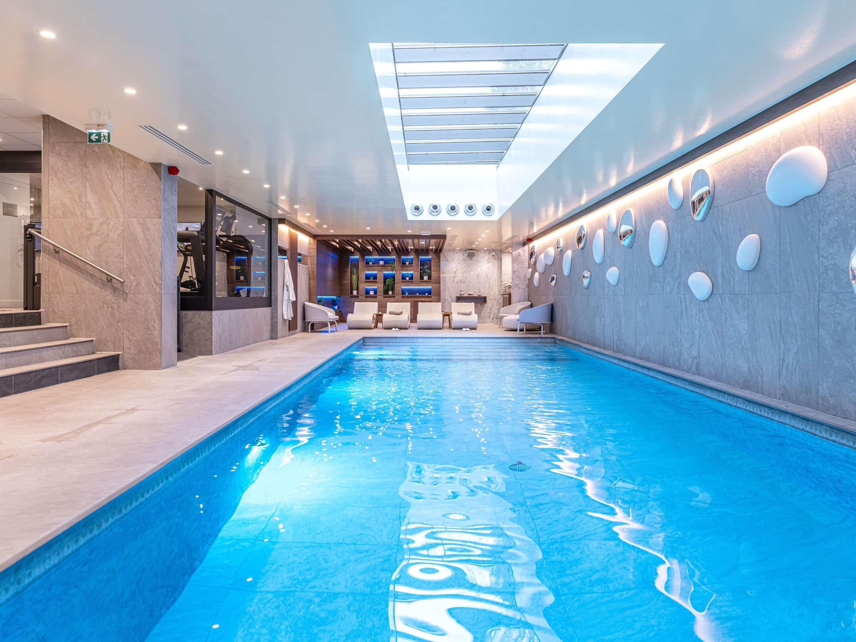 Piscina interior moderna com vista clara do teto, área de estar e escadaria que leva a um andar superior.