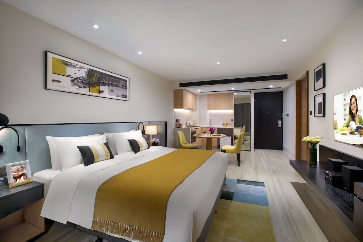 Quarto de hotel com cama, mesa de cabeceira, abajur, moldura e escrivaninha com cadeiras.
