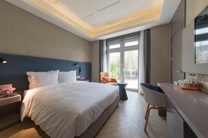 Quarto de hotel moderno com uma cama grande, uma escrivaninha, uma cadeira e vista para o exterior.