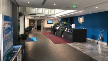 Um hall de hotel com uma mesa de recepção, um tapete vermelho e uma tela de televisão.