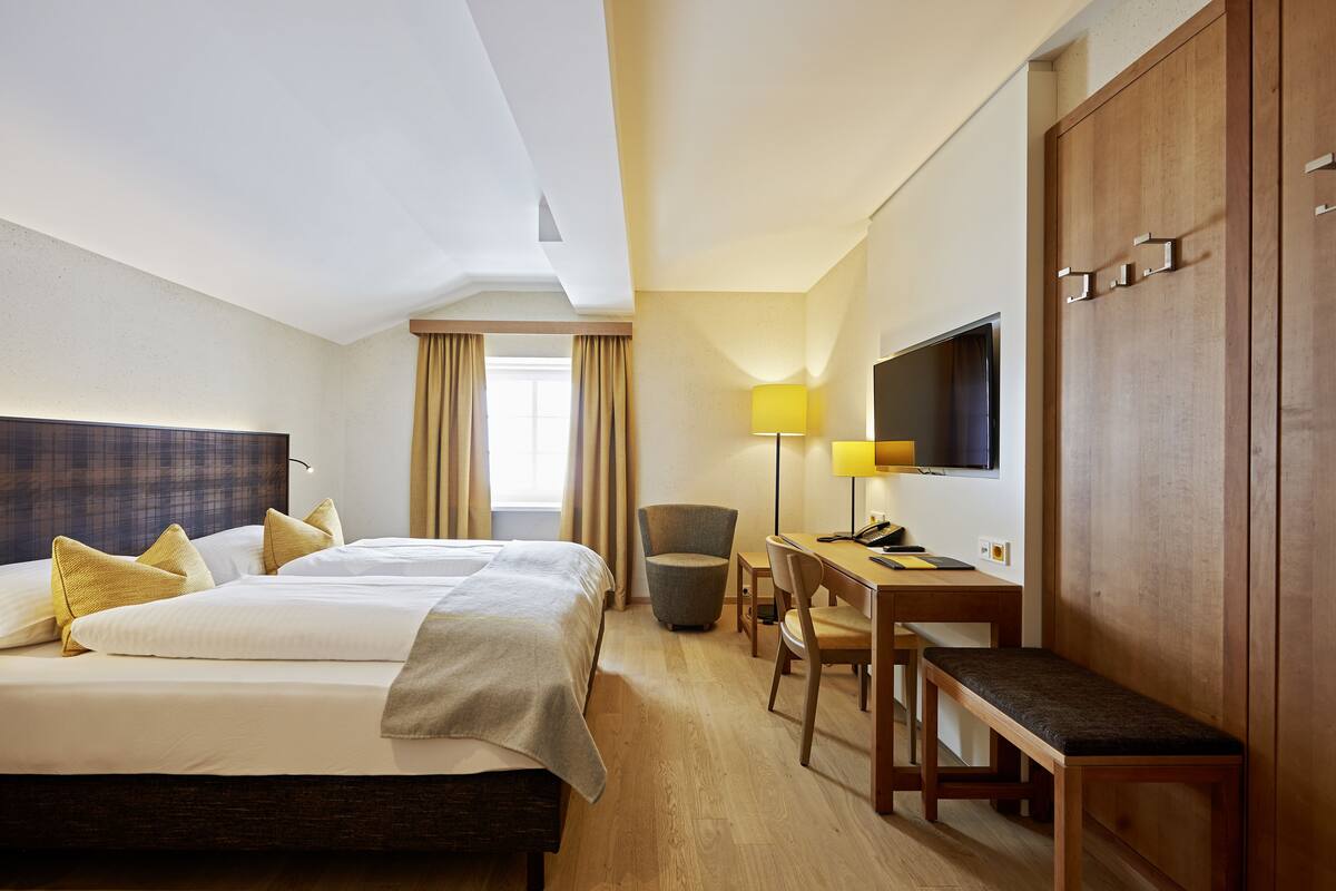 Quarto de hotel com uma cama grande, uma escrivaninha com cadeira, televisão e guarda-roupa.