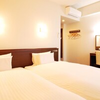 Quarto de hotel com cama de casal, cabeceira de madeira, aparelho de ar condicionado, mesa de cabeceira e cabideiro.
