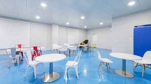 Uma sala de conferência com mesas e cadeiras redondas, paredes brancas e chão azul.