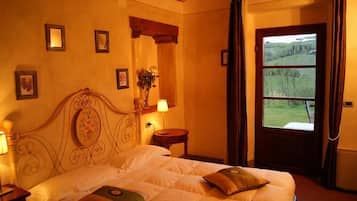Quarto com cama, mesa de cabeceira, luminária, pequena mesa com um vaso e janela com vista para o verde.