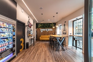 Interior moderno de um hostel com máquina de vendas automática, sofá e parede de madeira com plantas.