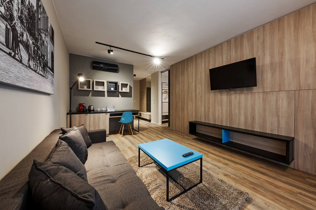Uma sala de estar moderna com um sofá, uma mesa de centro azul e uma televisão fixada na parede.