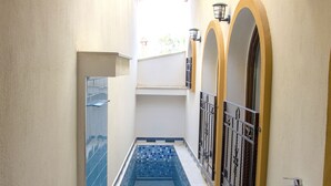 Uma área de piscina estreita com chão em mosaico, escada metálica e uma pia pequena com espelho.