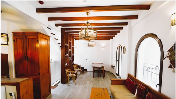 Uma sala de estar com móveis de madeira, um sofá, uma mesa de jantar e uma escada.