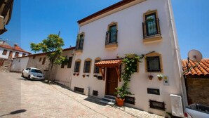 Um edifício de dois andares com telhado em telhas, entrada central com porta de madeira e pequena varanda.