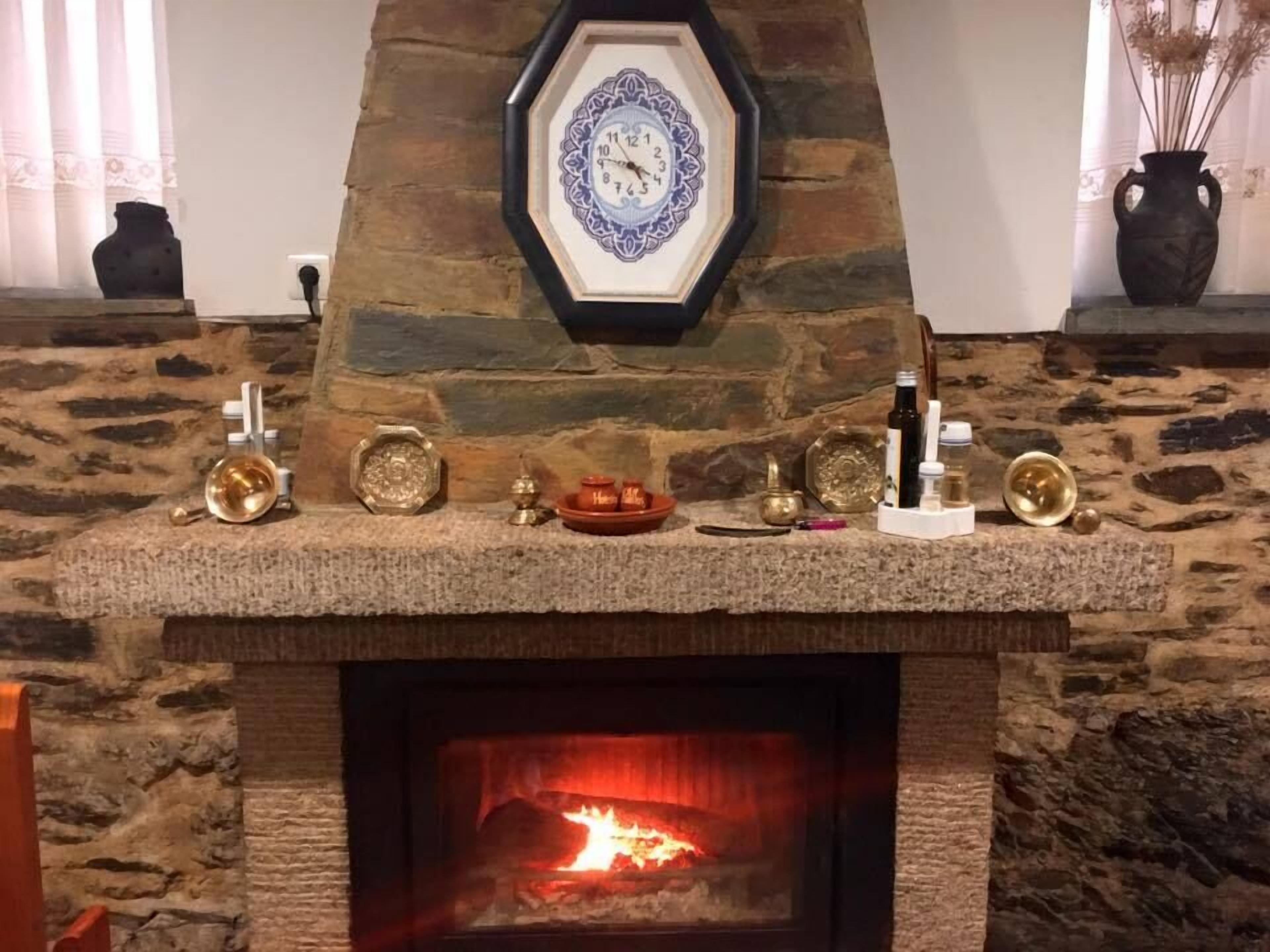 Lareira de pedra com um relógio em cima, rodeada por vários objetos decorativos.