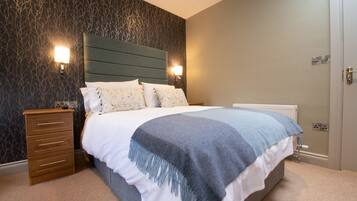 Quarto com cama, mesas de cabeceira, cômoda e luminária na parede.