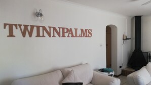 Uma sala de estar com um sofá bege, uma almofada preta e uma placa na parede com a inscrição TWINNPALMS.