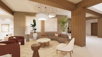 Uma sala de estar moderna com um sofá seccional, uma mesa de centro redonda e uma poltrona branca. Há duas luminárias pendentes, uma planta grande e uma obra de arte abstrata emoldurada na parede.