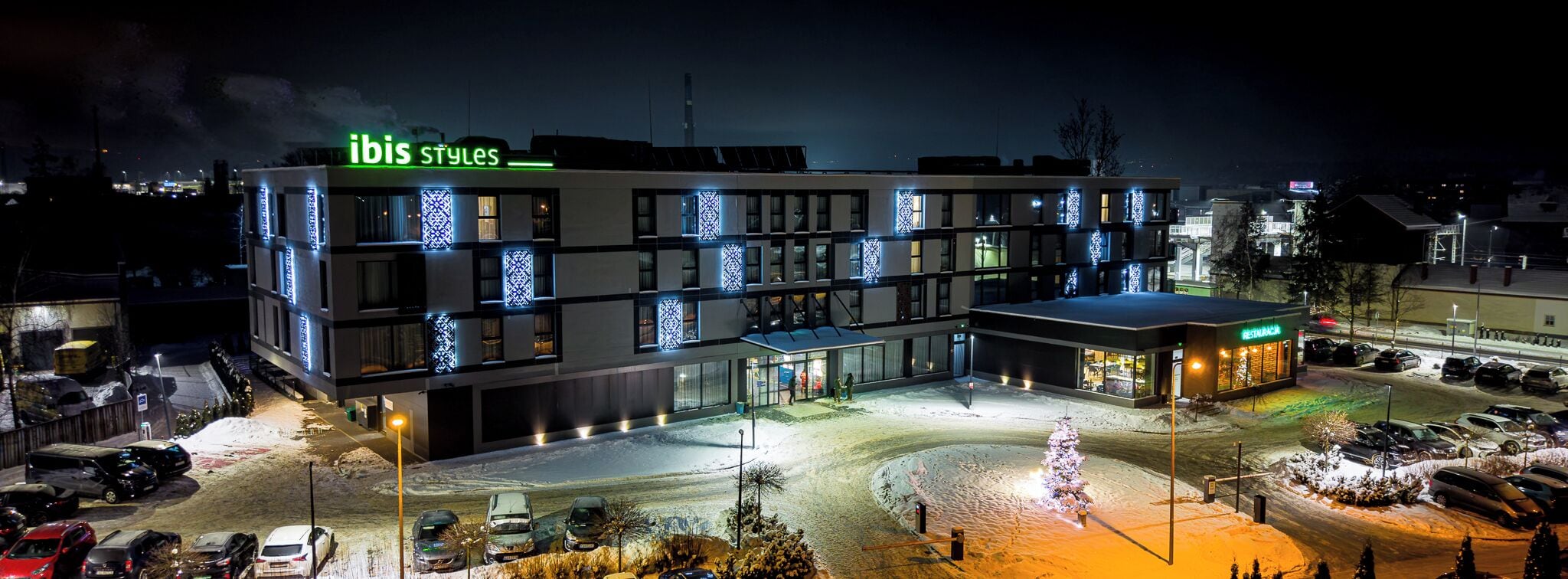 Um hotel moderno com uma placa indicando "ibis styles" e uma área de estacionamento coberta de neve.