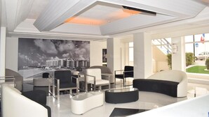 Um lounge moderno com mesa de centro de vidro, assentos confortáveis e um grande mural em preto e branco retratando uma paisagem urbana.