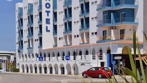 Um hotel com várias varandas, entrada central com arcos e um céu azul límpido.