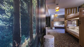 Quarto com um mural de floresta, beliches, uma mesa redonda e um tapete estampado.