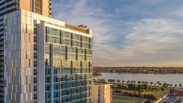 Um hotel moderno com fachada de vidro, situado perto de uma orla com vista para o horizonte da cidade.