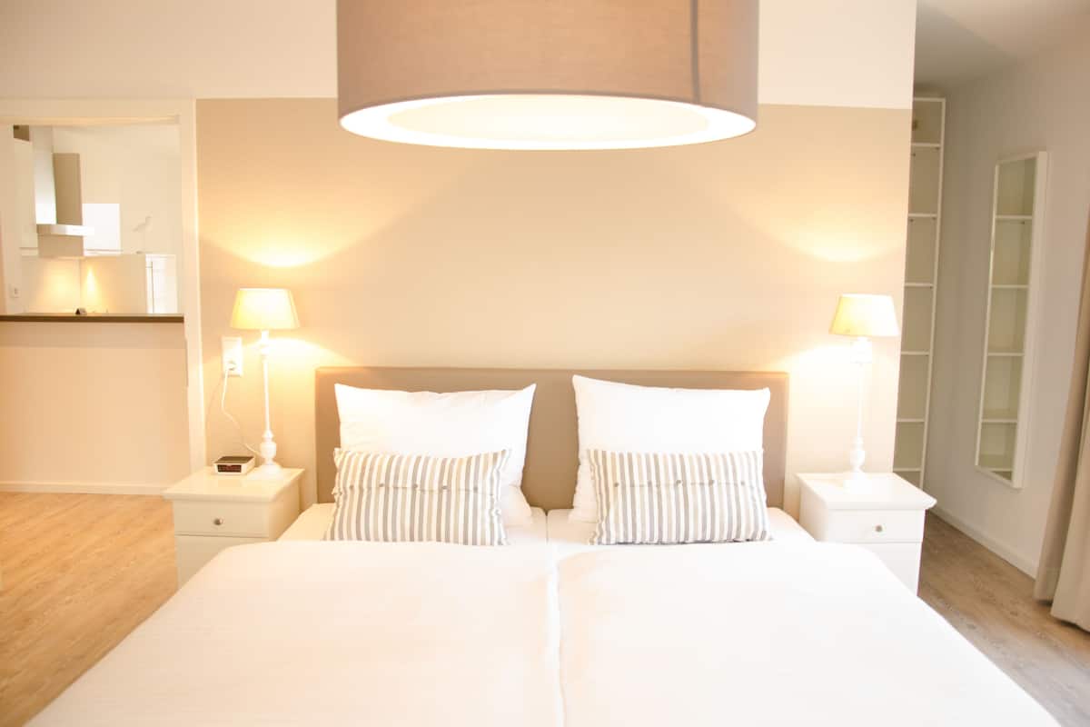 Quarto de hotel com uma cama grande, duas mesas de cabeceira com luminárias, um espelho e vista para um corredor.