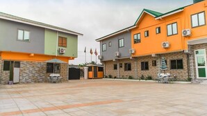 Pátio com edifícios de dois andares, mesas ao ar livre e bandeiras.