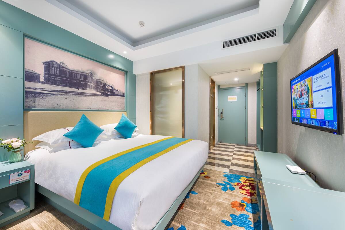 Quarto de hotel com uma cama grande, uma escrivaninha, uma TV e um quadro na parede.