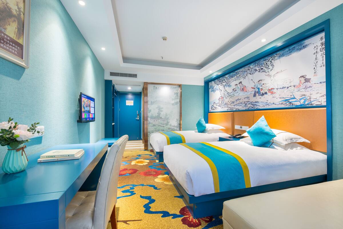 Quarto de hotel com duas camas, uma escrivaninha e um grande painel decorativo.