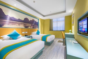 Quarto de hotel com duas camas, uma escrivaninha, uma televisão e uma pintura de uma paisagem de montanha.