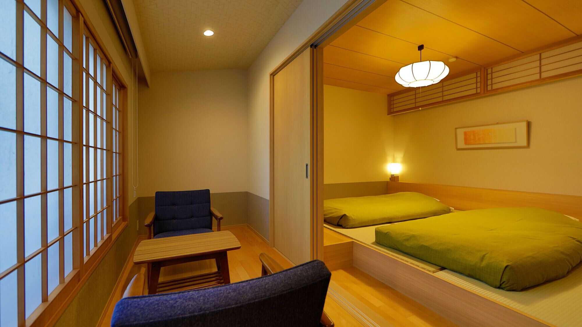 Quarto tradicional em estilo japonês, com piso de tatame, uma mesa baixa, uma cadeira e uma cama com roupa de cama verde.