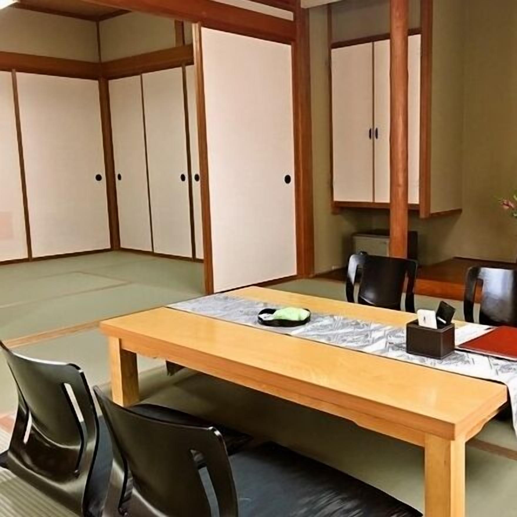 Quarto em estilo japonês tradicional, com tatames, uma mesa de madeira baixa e cadeiras pretas.