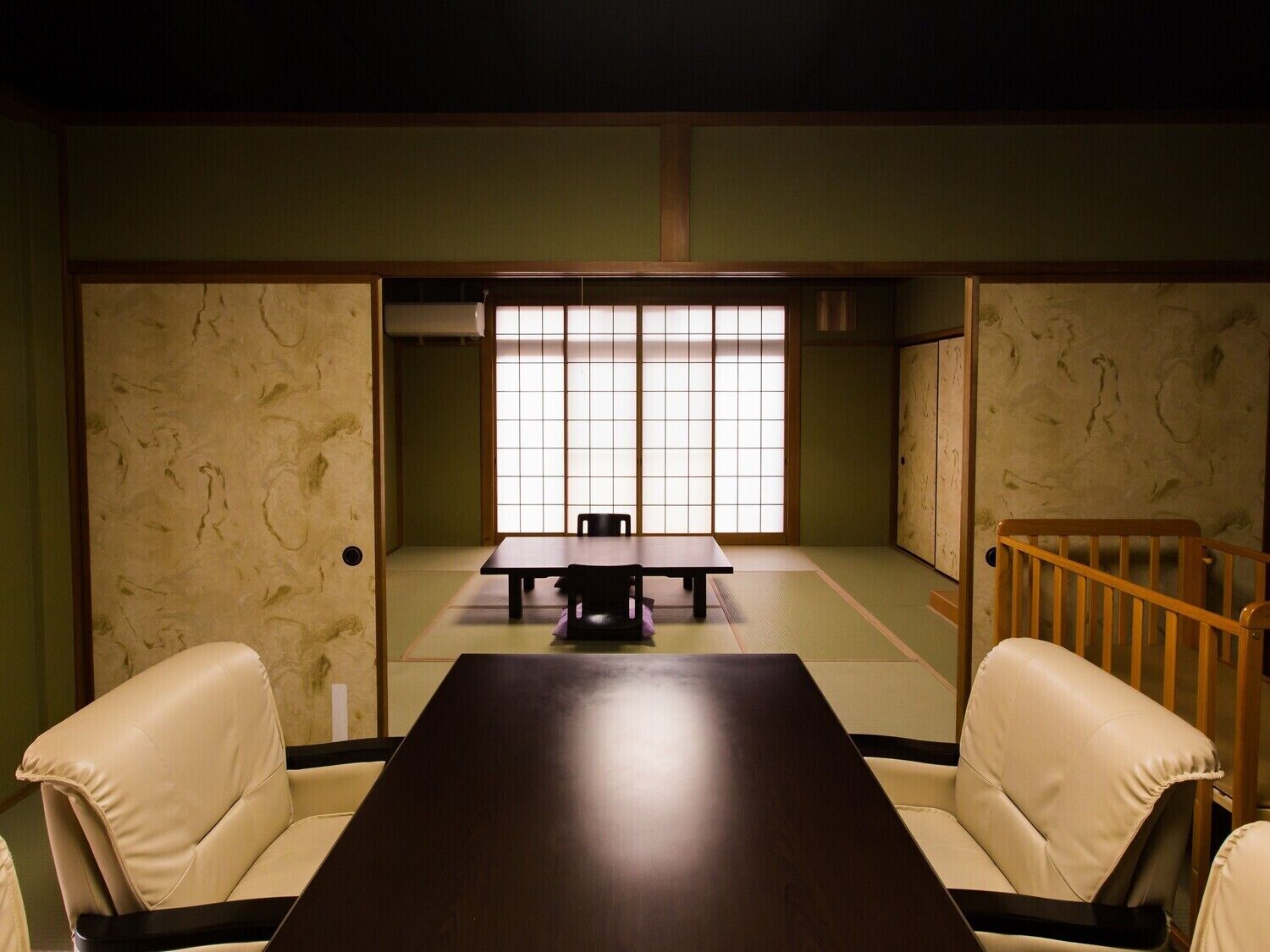 Um quarto japonês tradicional com tatames, uma mesa baixa e duas cadeiras estofadas.