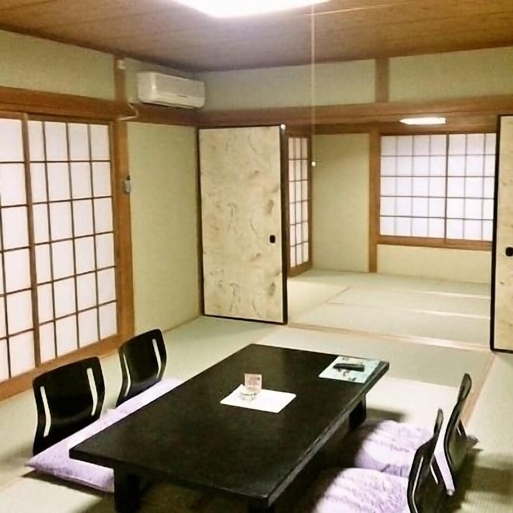 Um quarto japonês tradicional com tatames, painéis shoji e uma mesa baixa com cadeiras.