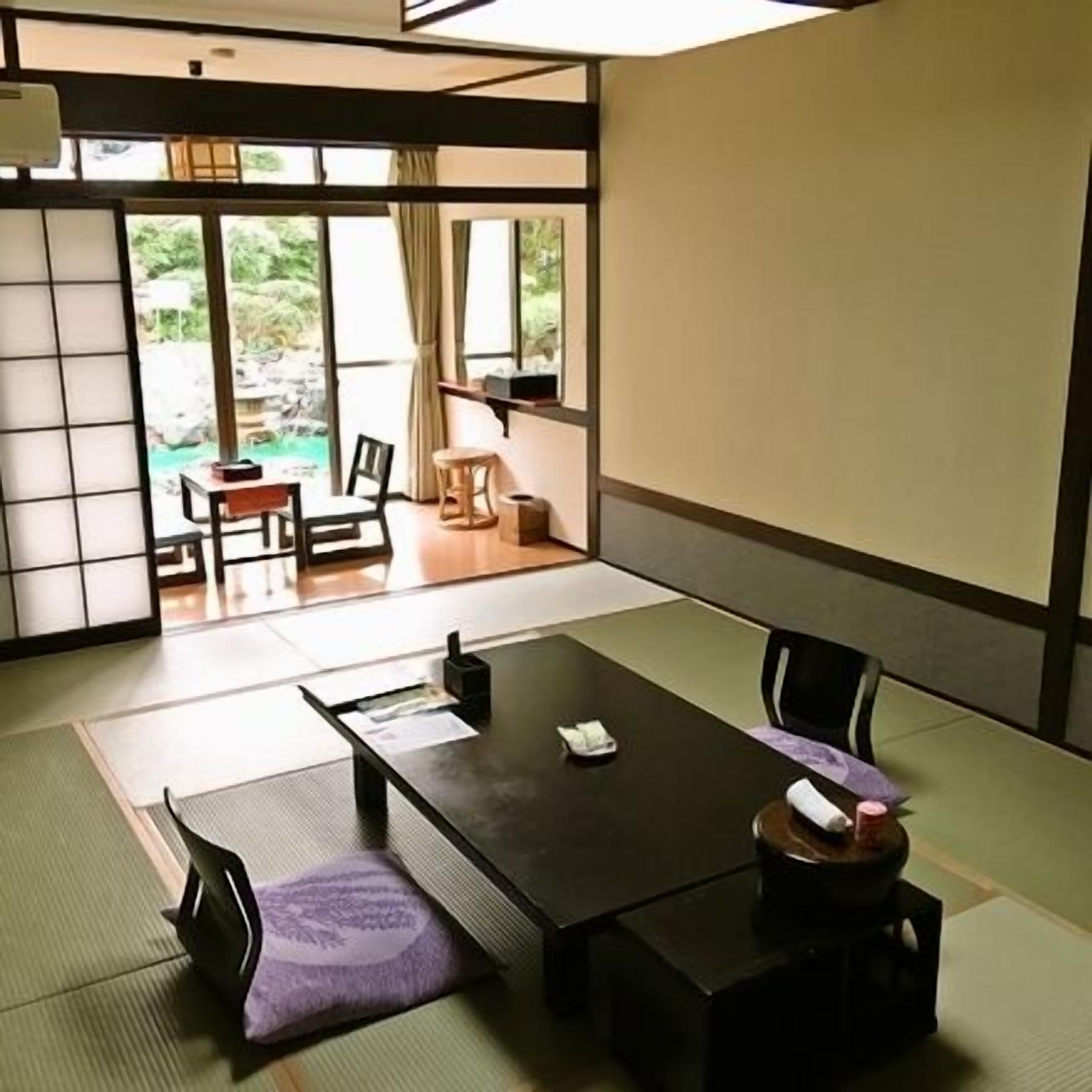Quarto tradicional japonês com tatames, uma mesa baixa com almofada e portas deslizantes para uma área externa.