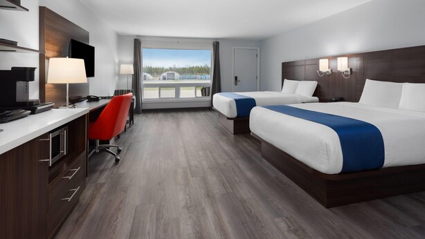 Quarto de hotel com duas camas, uma escrivaninha com computador, televisão e janela com vista para edifícios.