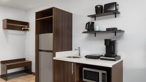 Uma cozinha compacta com micro-ondas embutido, cafeteira e moedor de café na bancada.