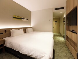 Quarto de hotel moderno com uma cama grande, televisão de tela plana, cabeceira de madeira e piso coberto por carpete.