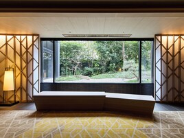 Um quarto com uma janela grande, um banco e um abajur.