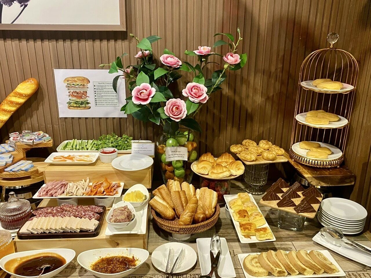 Buffet com diversos alimentos, incluindo pão, doces e um vaso decorativo com flores.