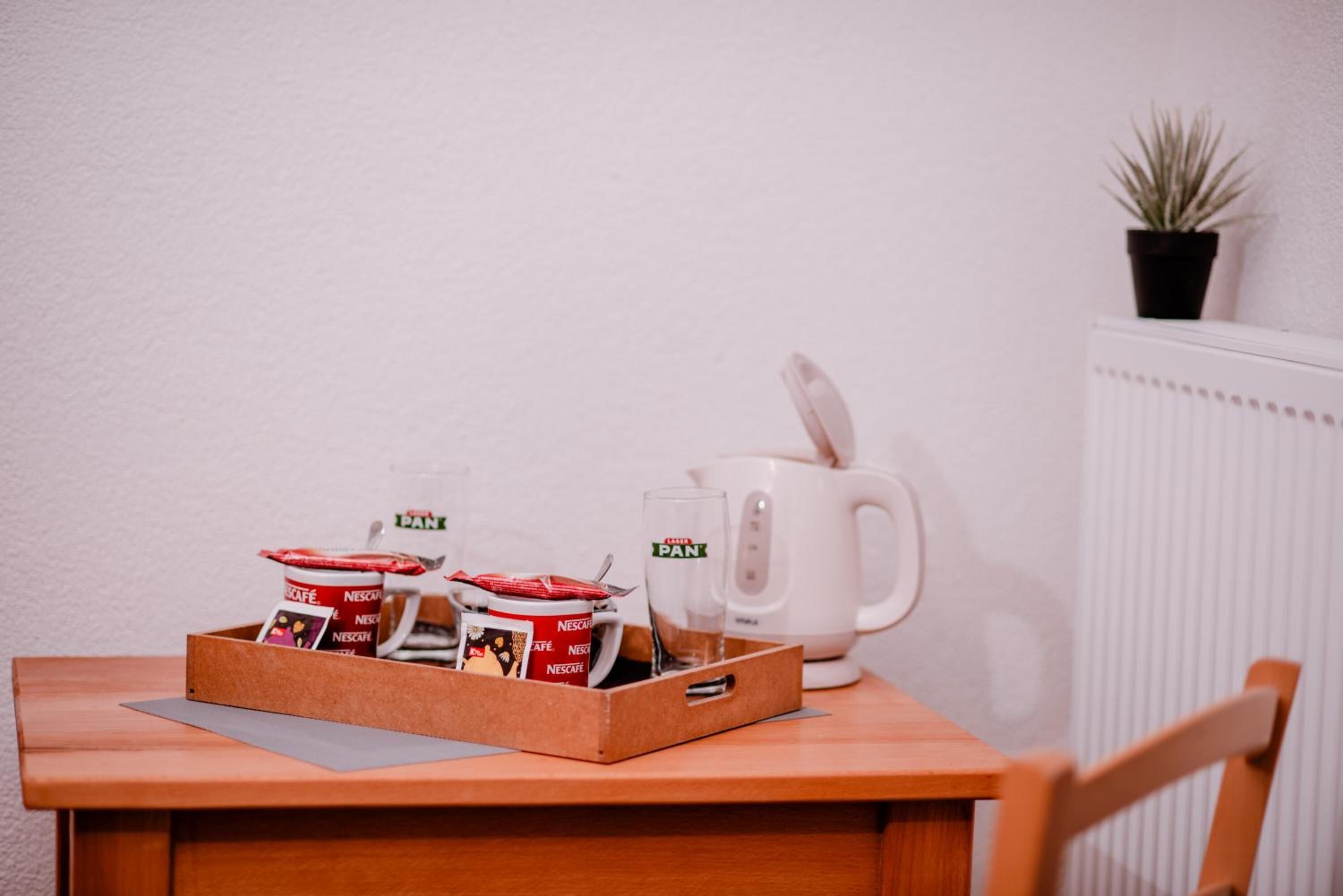 Uma mesa de madeira com uma bandeja contendo vários copos de Nescafé e uma cafeteira branca.