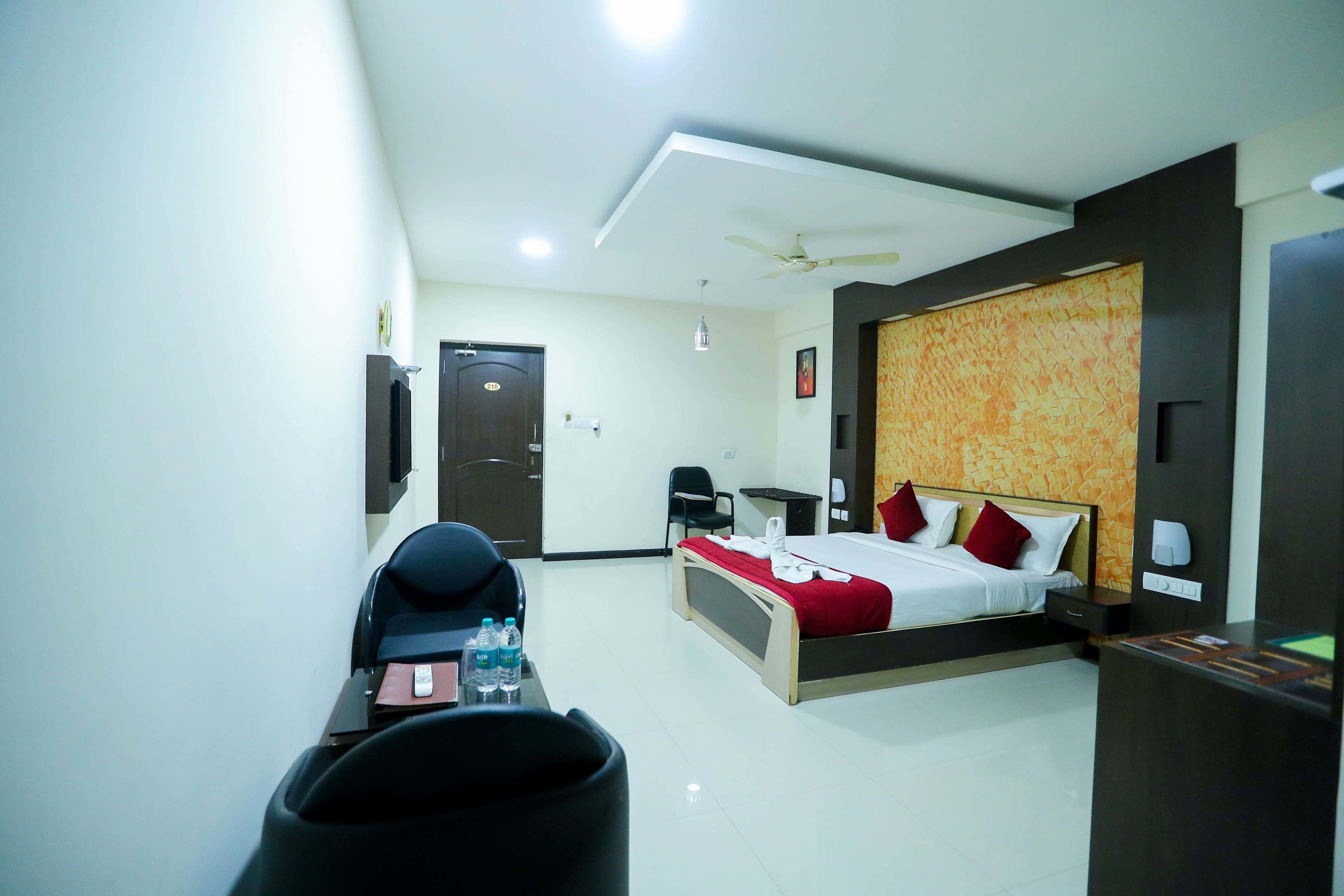 Quarto de hotel com cama, escrivaninha com cadeira, televisão e ventoinha no teto.