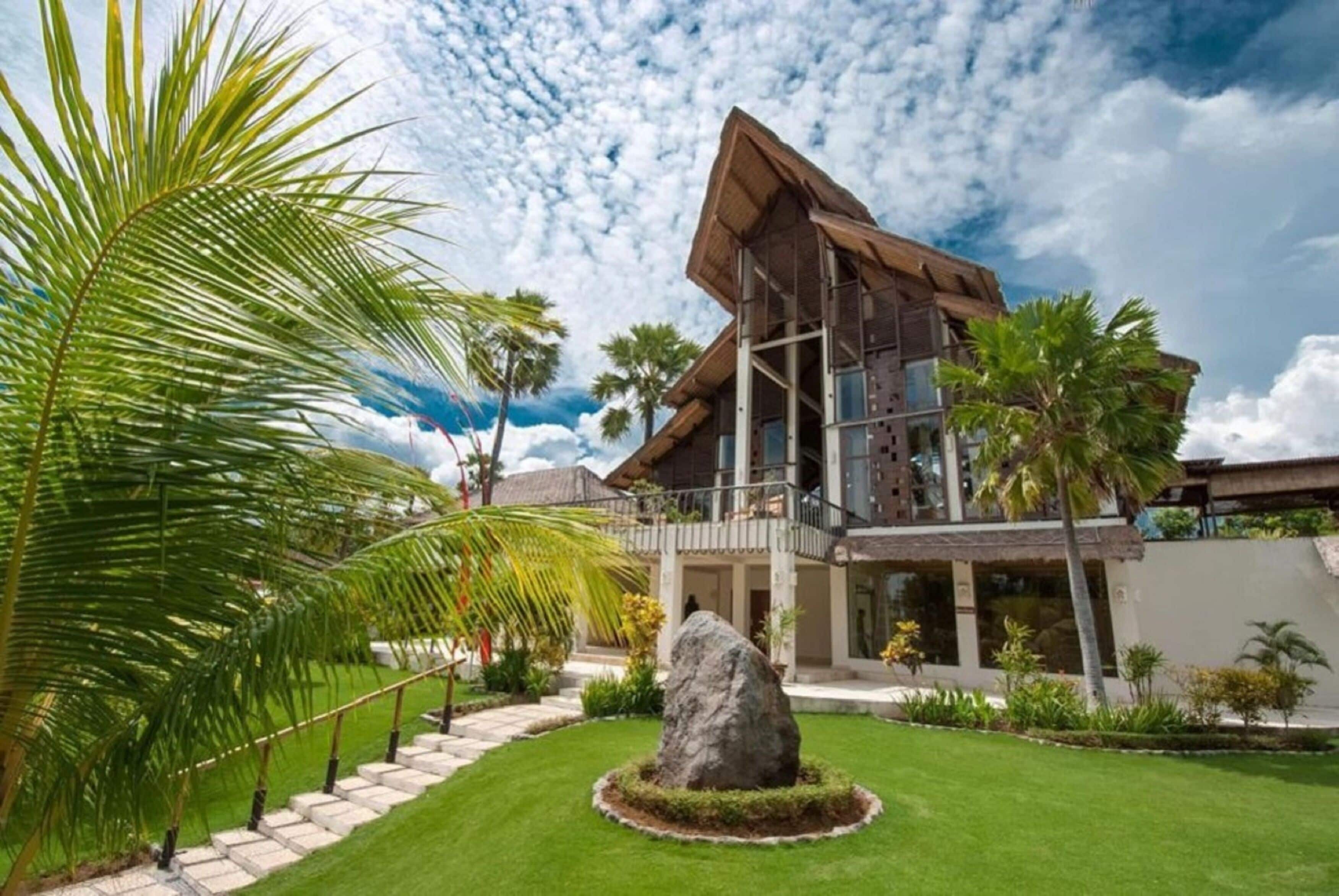 Uma casa moderna com uma varanda grande, cercada por um gramado bem cuidado e palmeiras.